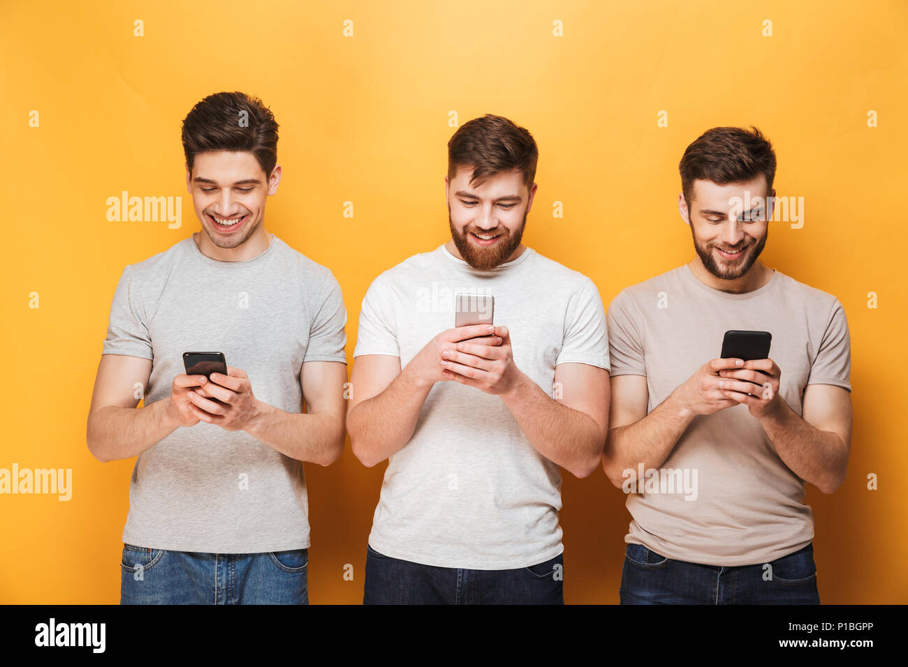 Three young smiling men using mobile phones isolated over yellow ...