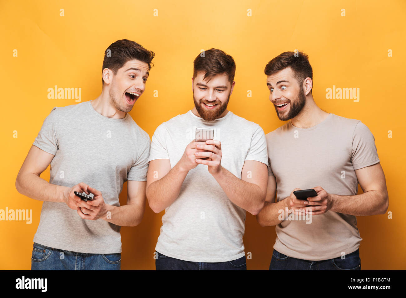 Three young smiling men using mobile phones isolated over yellow ...