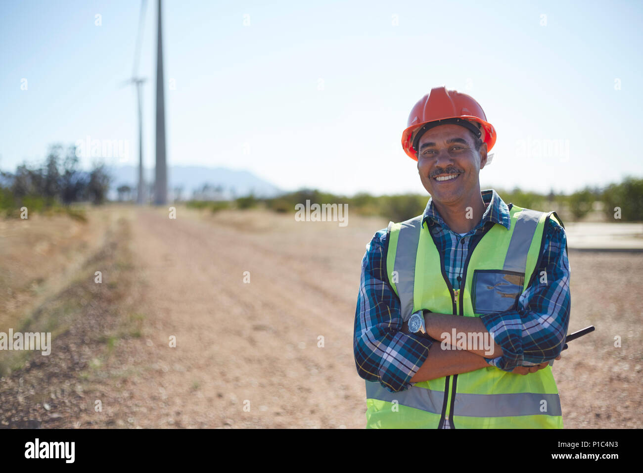 Portrait smiling engineer on dirt road at wind turbine power plant ...