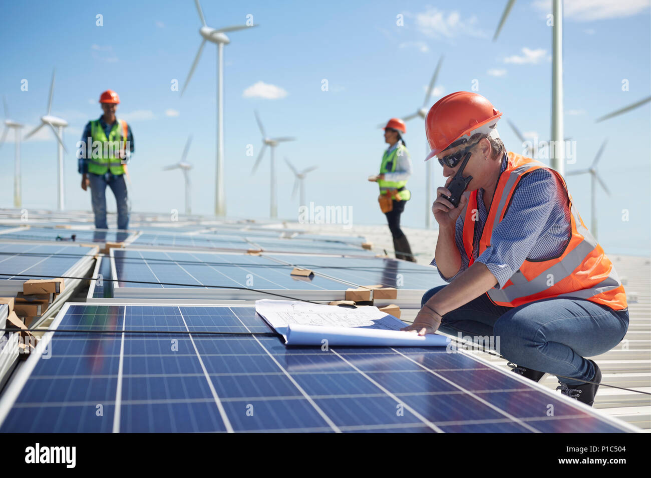 Engineer with walkie-talkie and blueprint at solar panel at sunny power ...