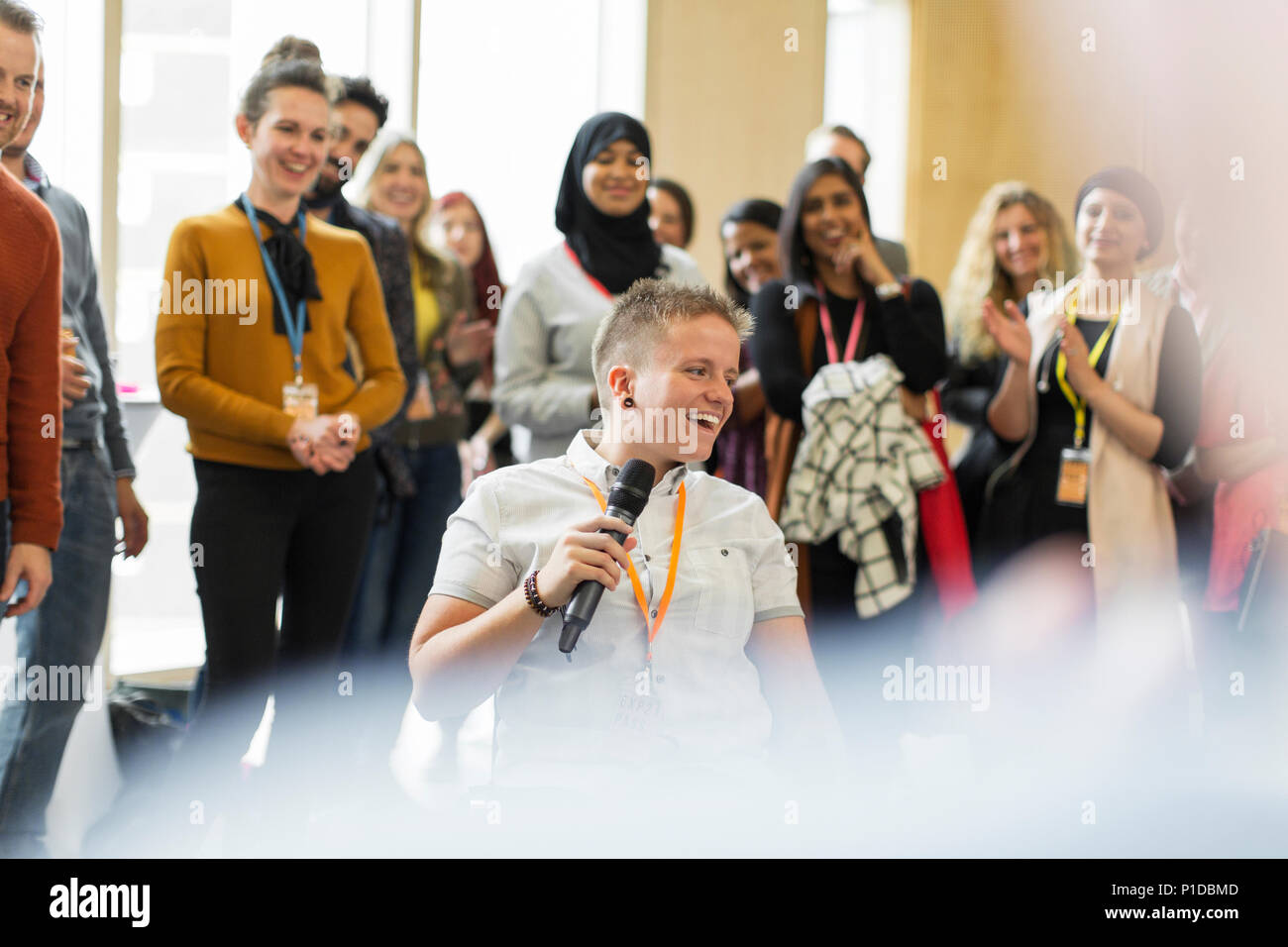 Conference audience clapping for smiling female speaker with microphone ...