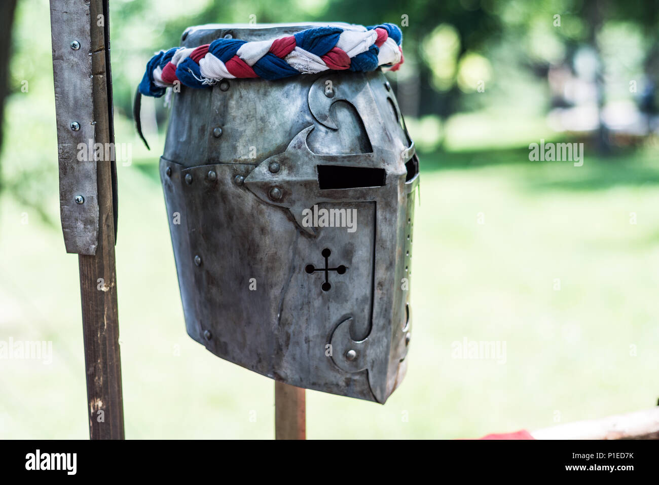 Iron helmet of the medieval knight on wooden stand with red, blue and ...