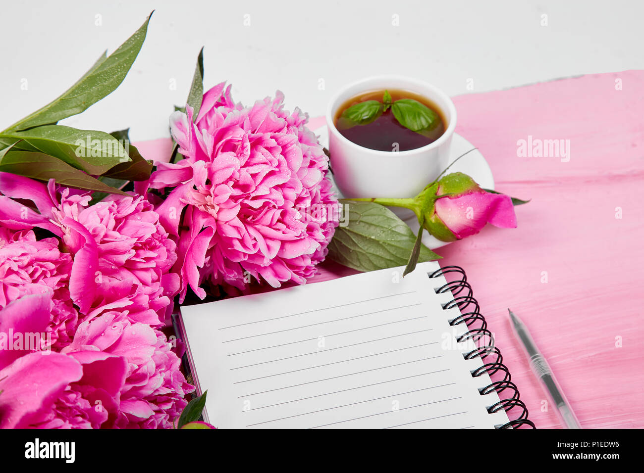 Peony flowers on pink background with note or diary and cup of coffee ...