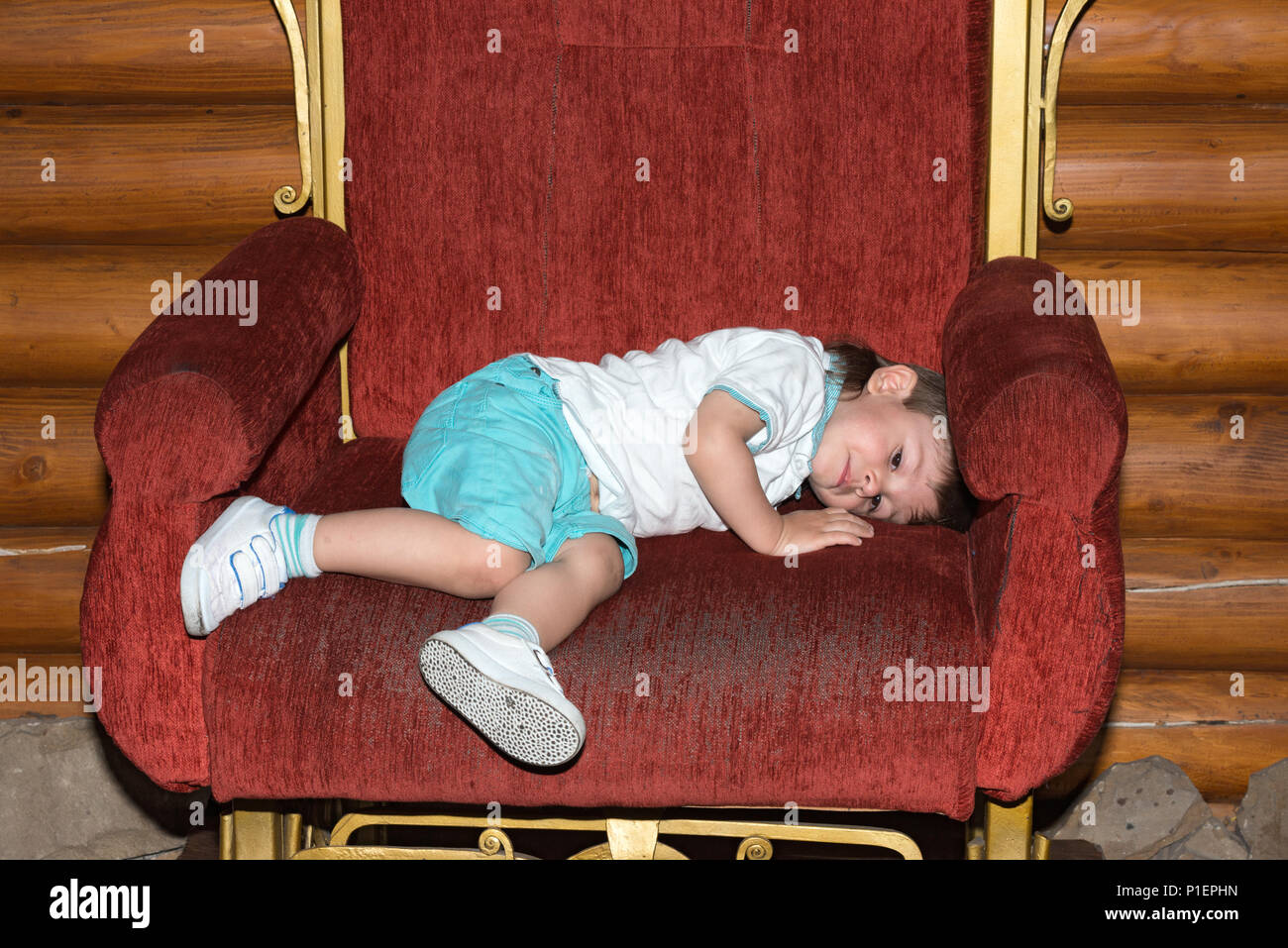 Little boy that tired and want to sleep lay down on the big red ...