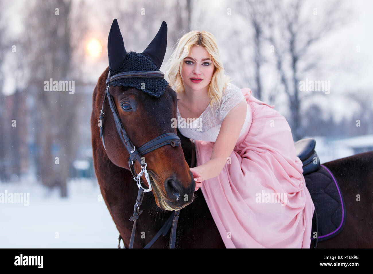 Young woman in rose dress riding her bay horse on winter field ...