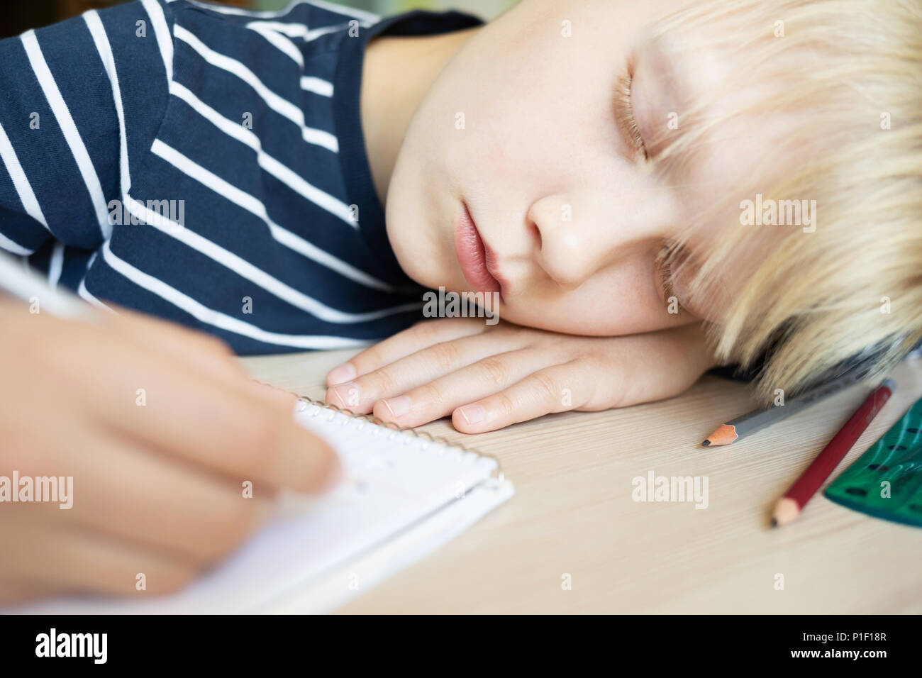 Boy sleeping on the desk while doing his homework in notebook. Close up ...