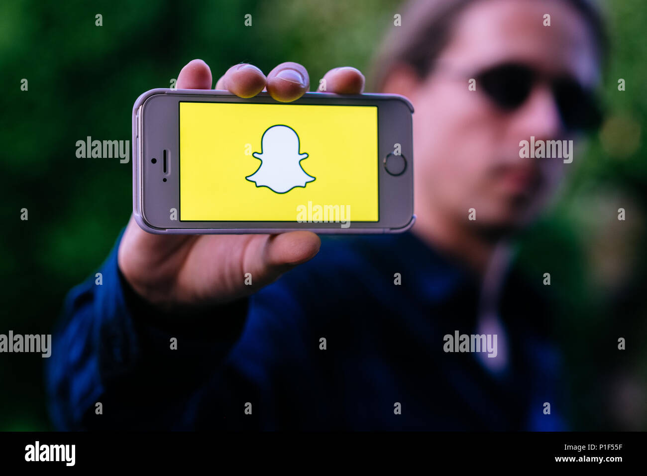 Closeup of serious young man with sunglasses holding white iPhone with ...