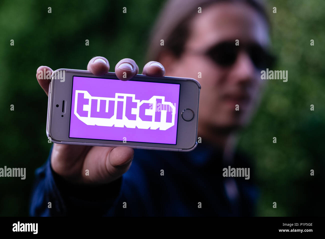Closeup of serious young man holding white iPhone with TWITCH LOGO on ...