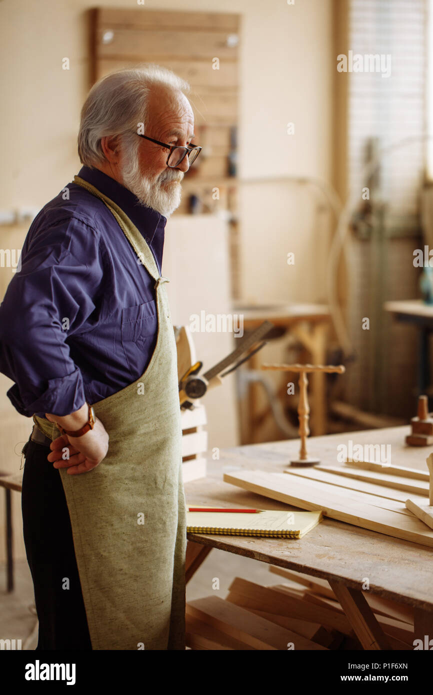 old carpenter standing with hands on hips after finishing his hard work ...