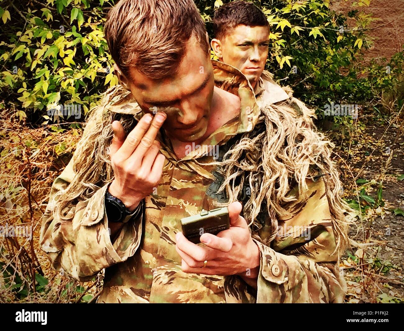 Spc. Brandon Miller (front), a sniper team spotter, applies face paint ...