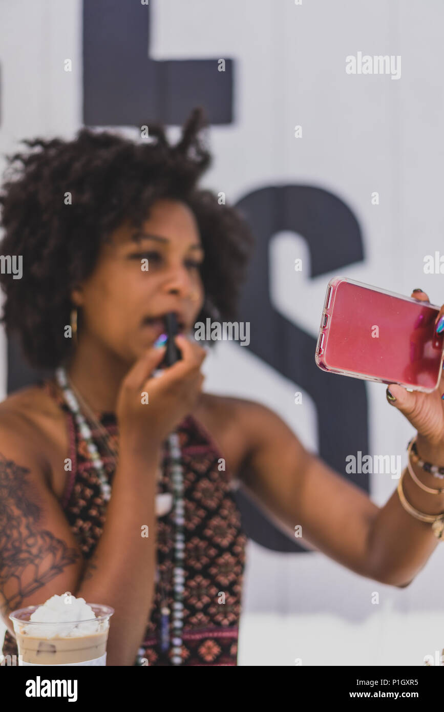 Stylish black woman using cell phone to apply lipstick Stock Photo - Alamy