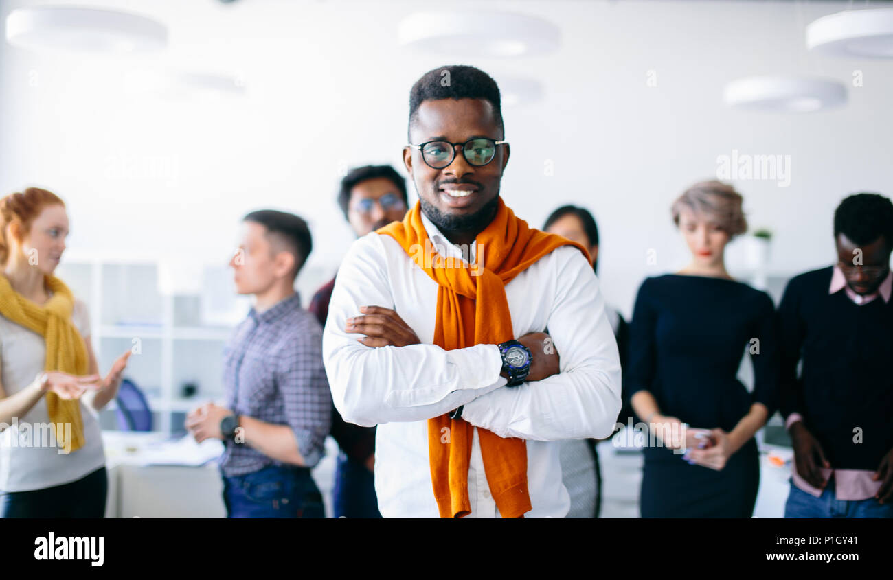 confident handsome black boss with crossed arms in front of co-workers ...