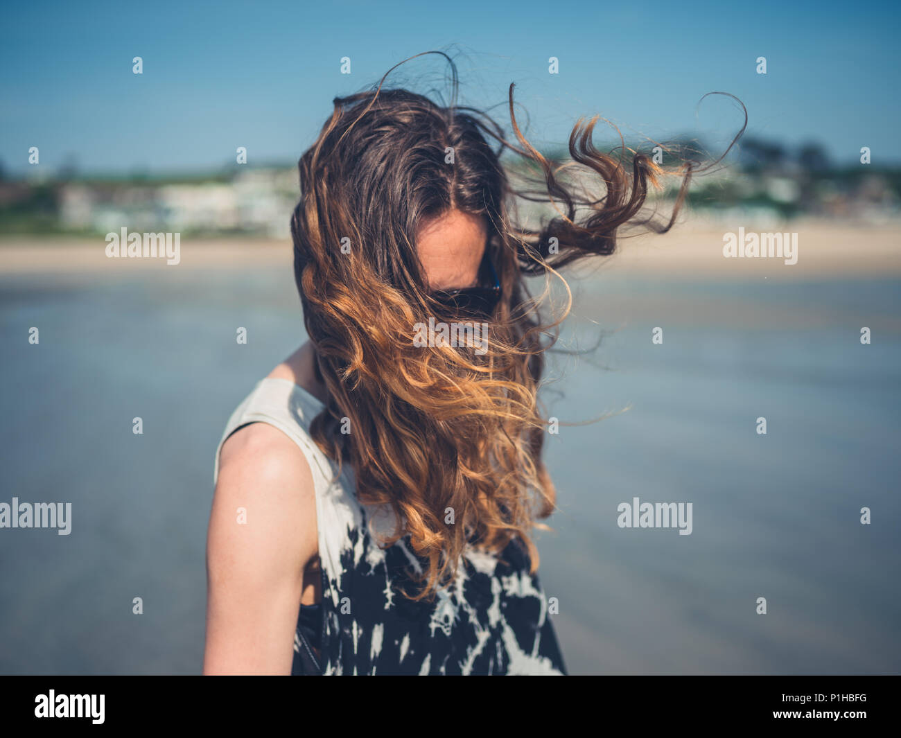A young woman is standing on the beach with her hair blowing in the ...