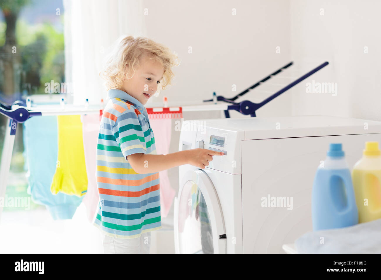 Child in laundry room with washing machine or tumble dryer. Kid helping ...