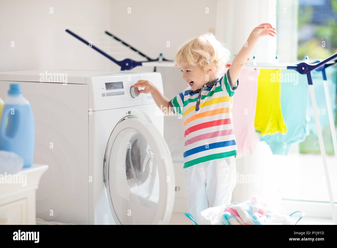 Child in laundry room with washing machine or tumble dryer. Kid helping ...