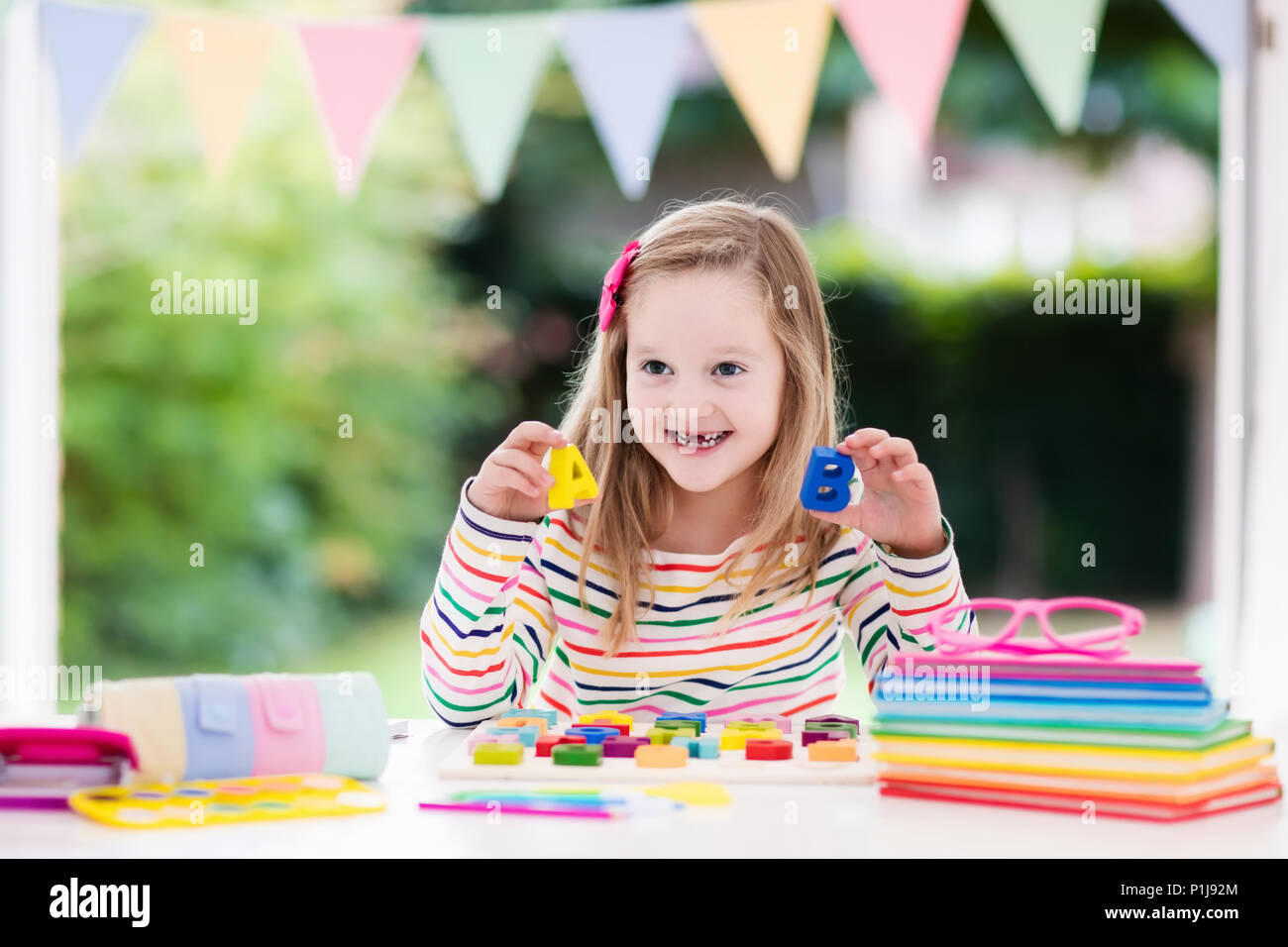 Child doing homework for school at white desk. Wooden educational abc ...