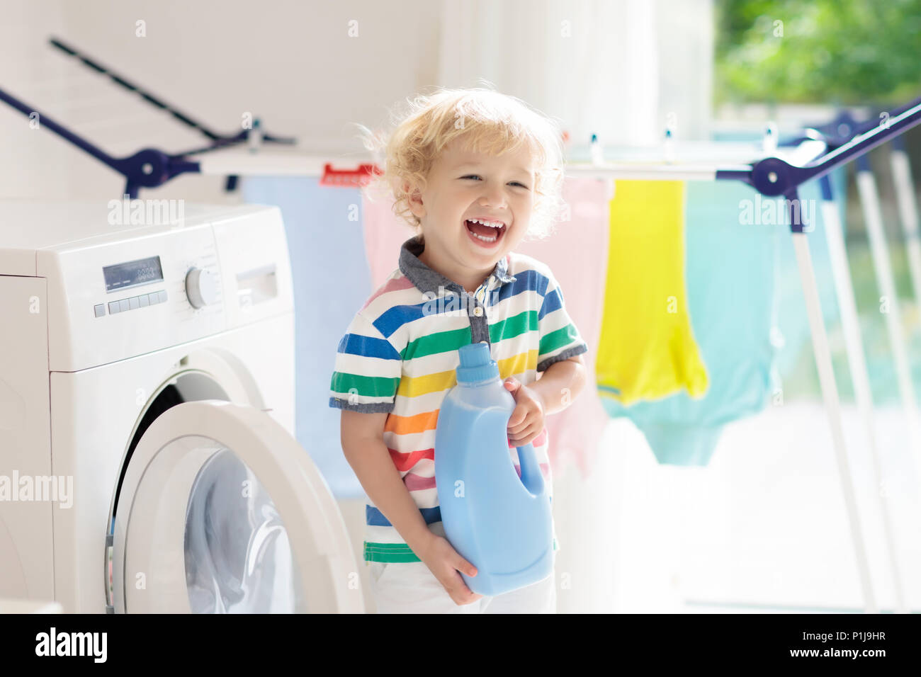 Child in laundry room with washing machine or tumble dryer. Kid helping ...