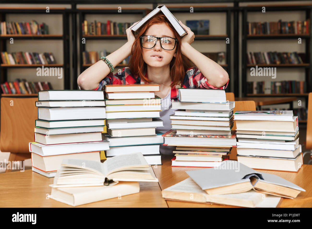 Frustrated teenage girl sitting at the library table with big stacks of ...