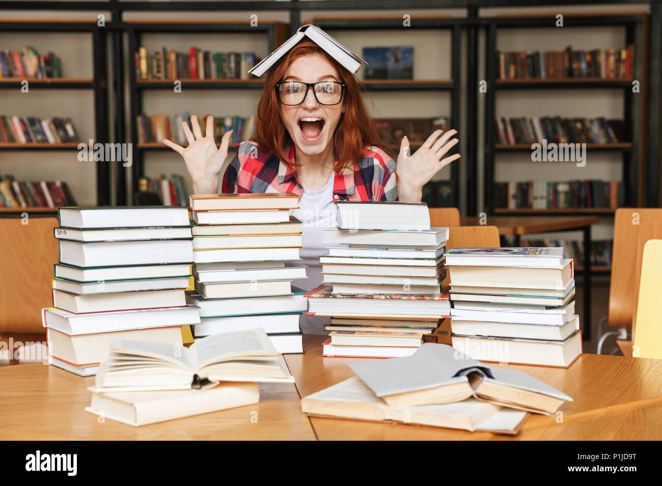 Excited teenage girl sitting at the library table with big stacks of ...