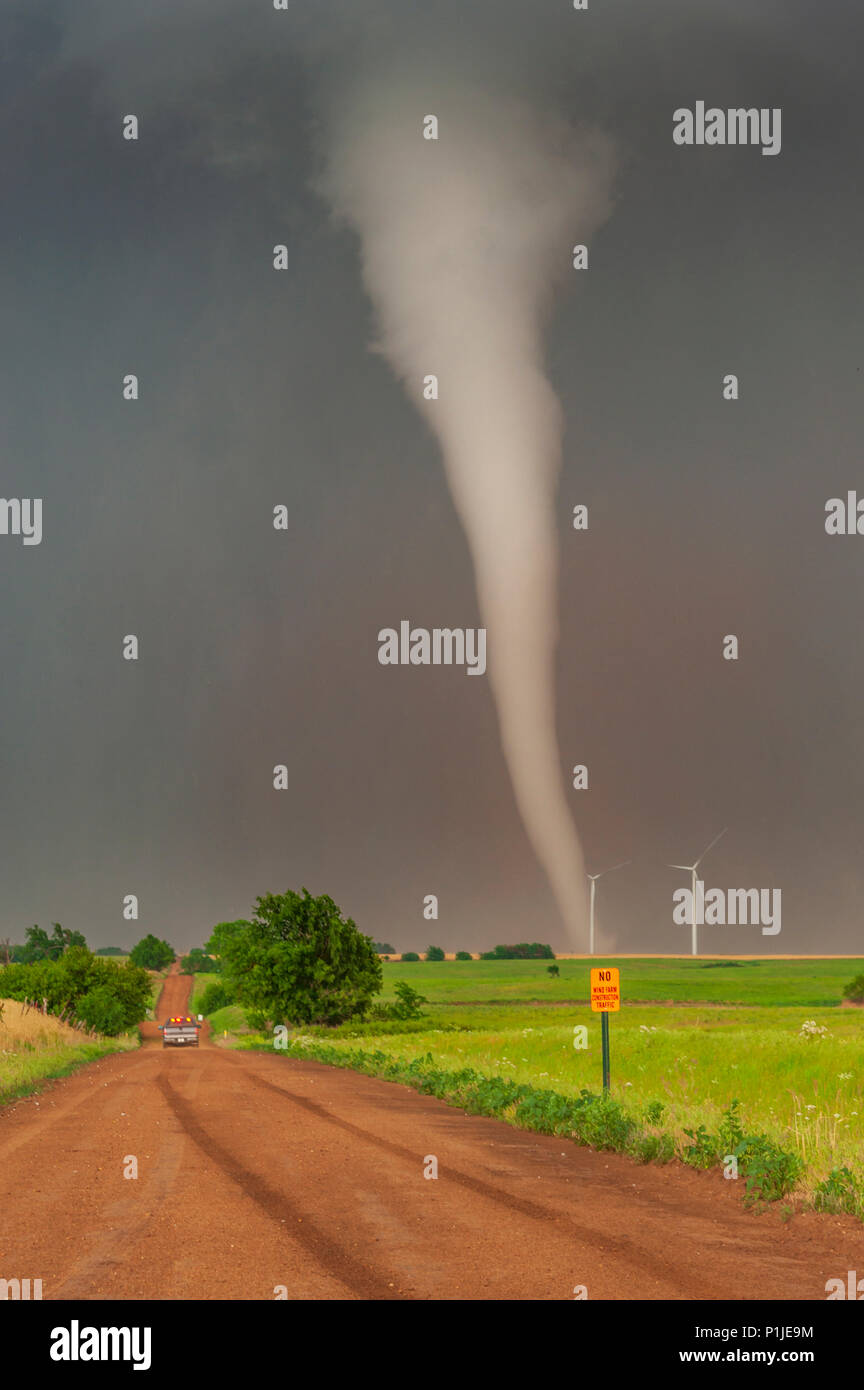 Pickup drives over mud road with a close tornado in a wind farm near ...