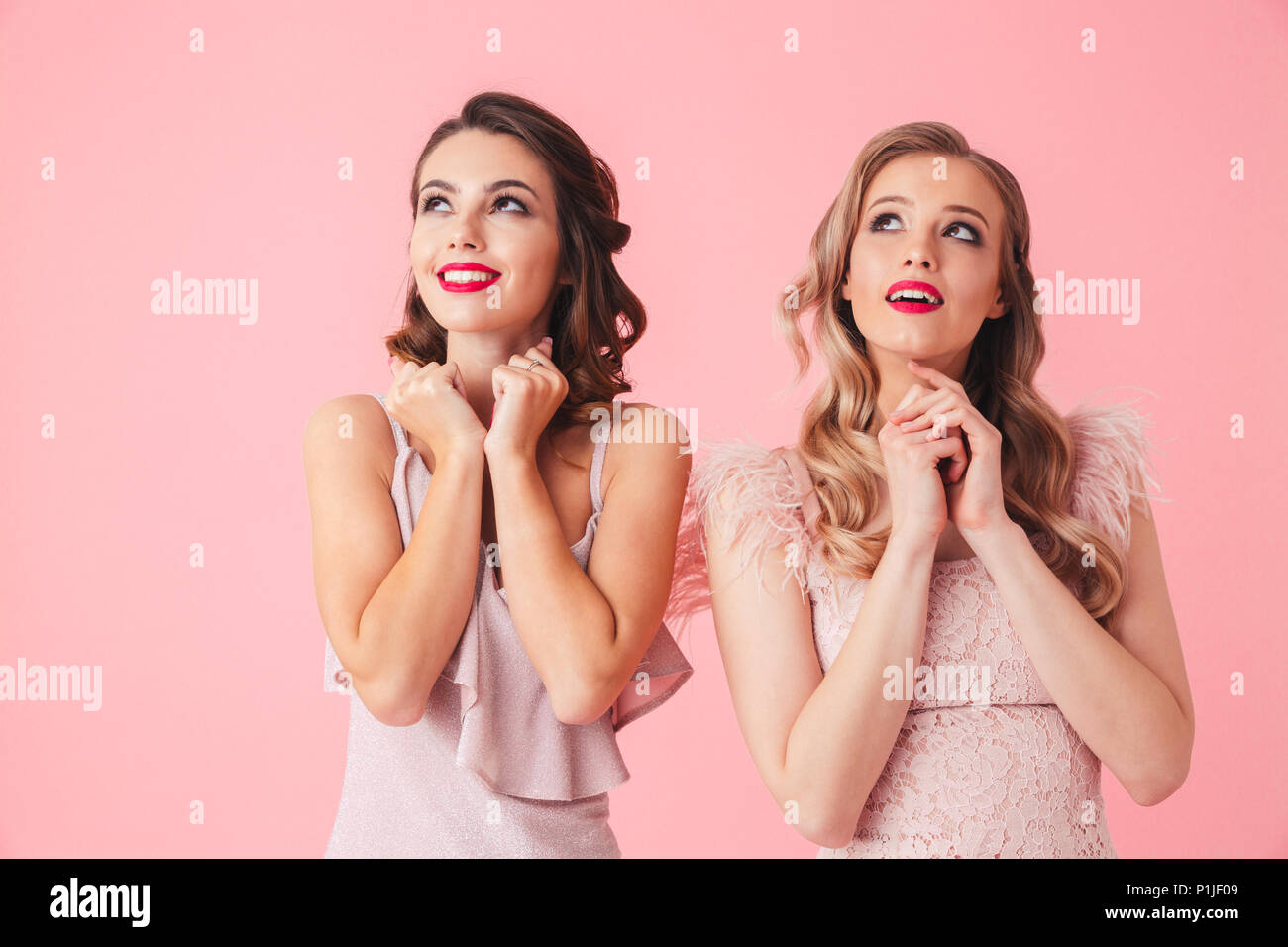 Two pensive intrigued women in dresses posing together with arms near ...
