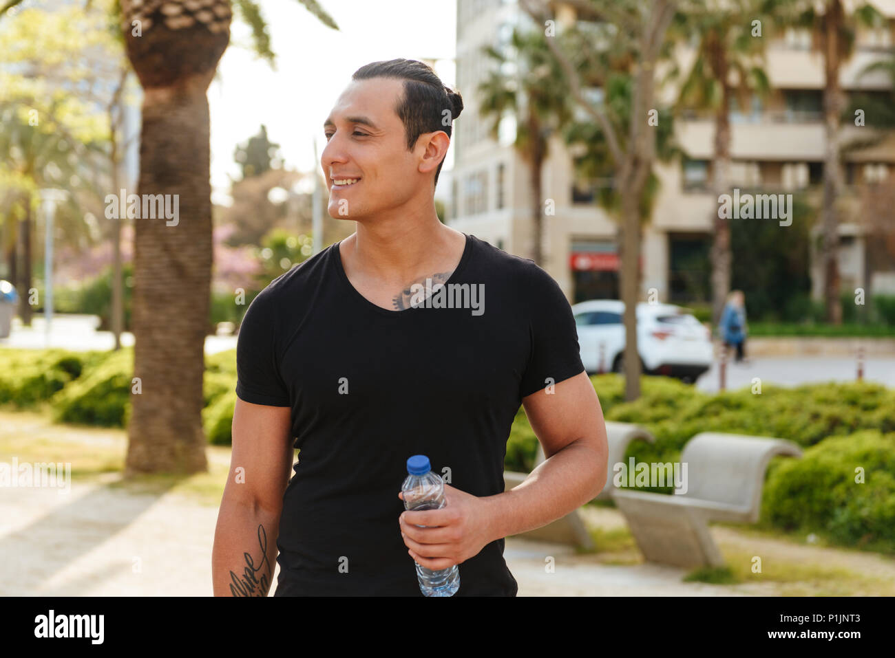 Image of cheerful young strong sports man walking outdoors with bottle ...