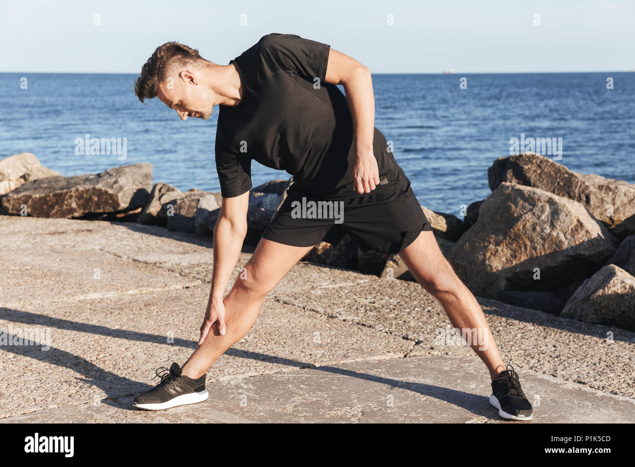 Handsome sportsman doing stretching exercises at the beach Stock Photo ...