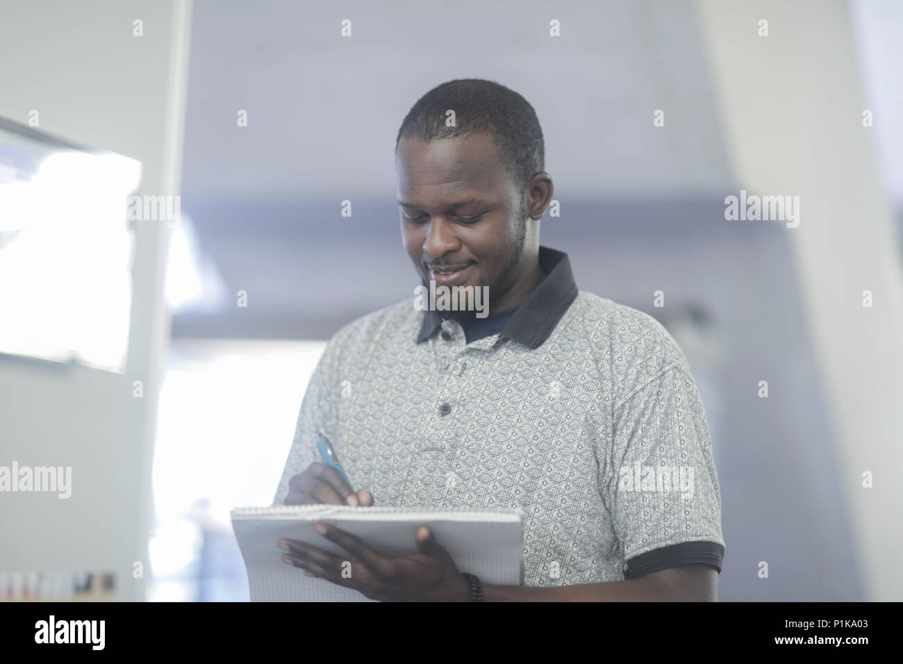 Man standing in office writing on a notepad Stock Photo - Alamy