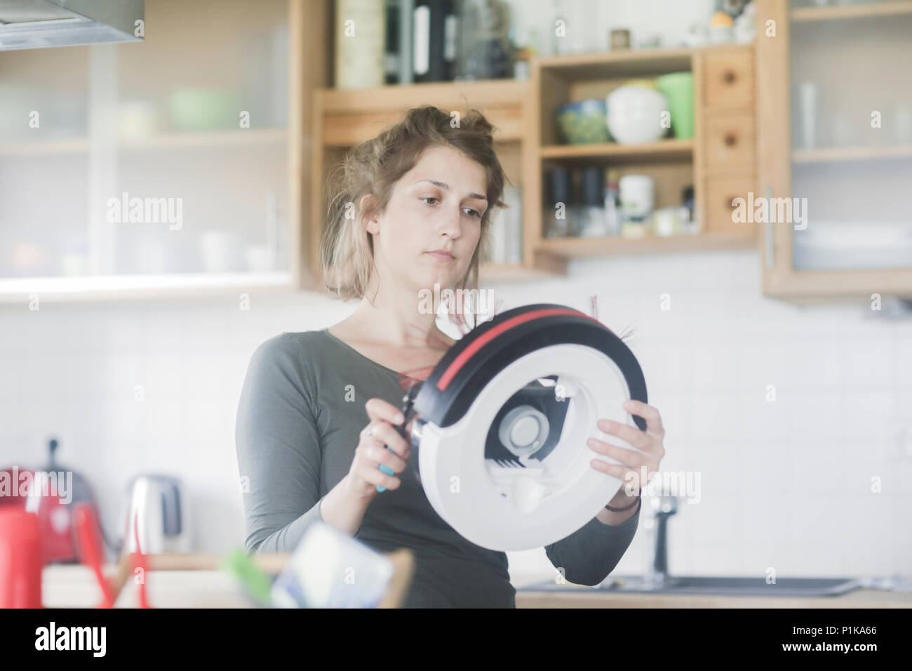 Woman standing in kitchen fixing a robotic vacuum cleaner Stock Photo ...