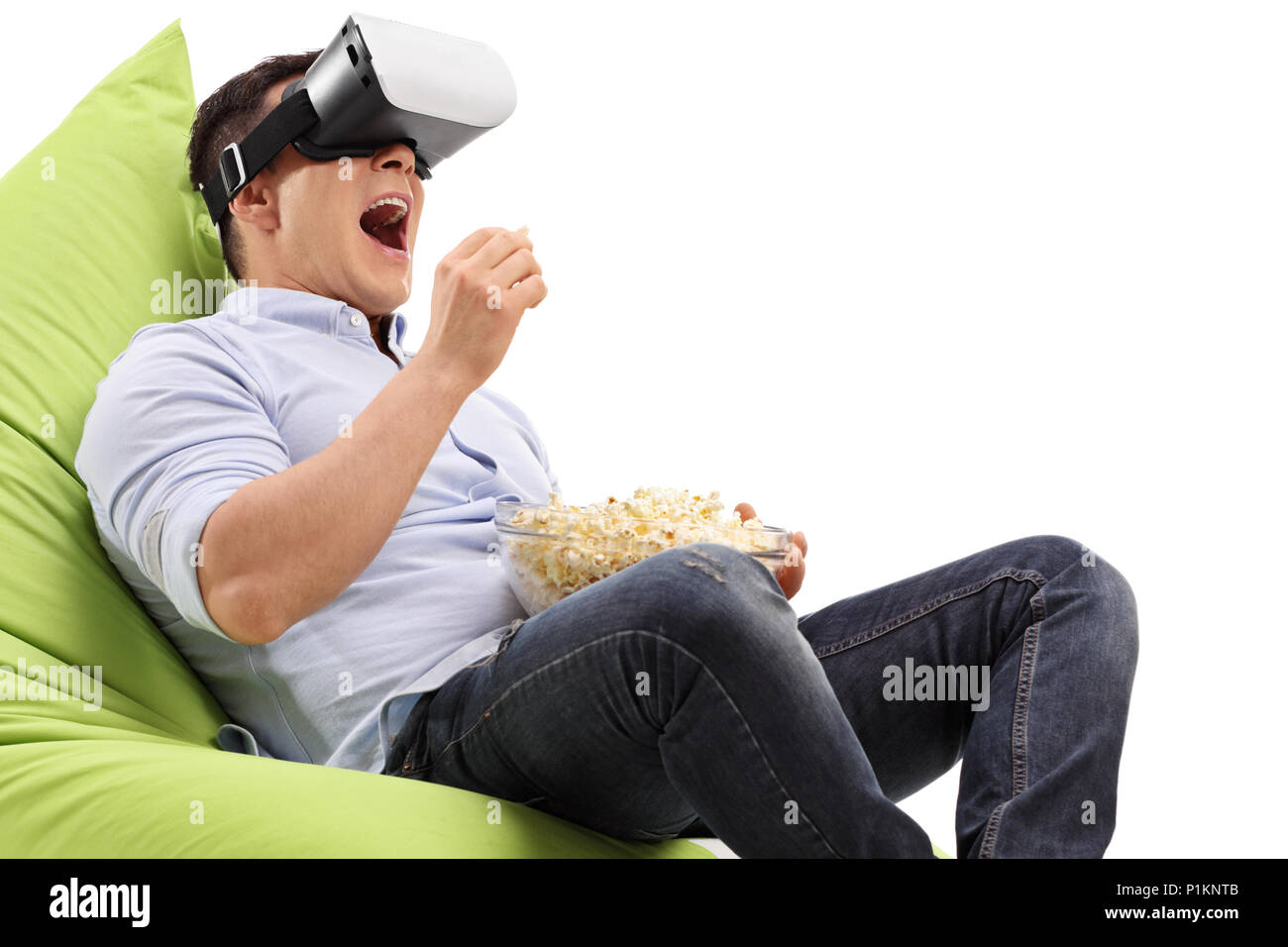 Young man using a VR headset and eating popcorn seated on a beanbag ...