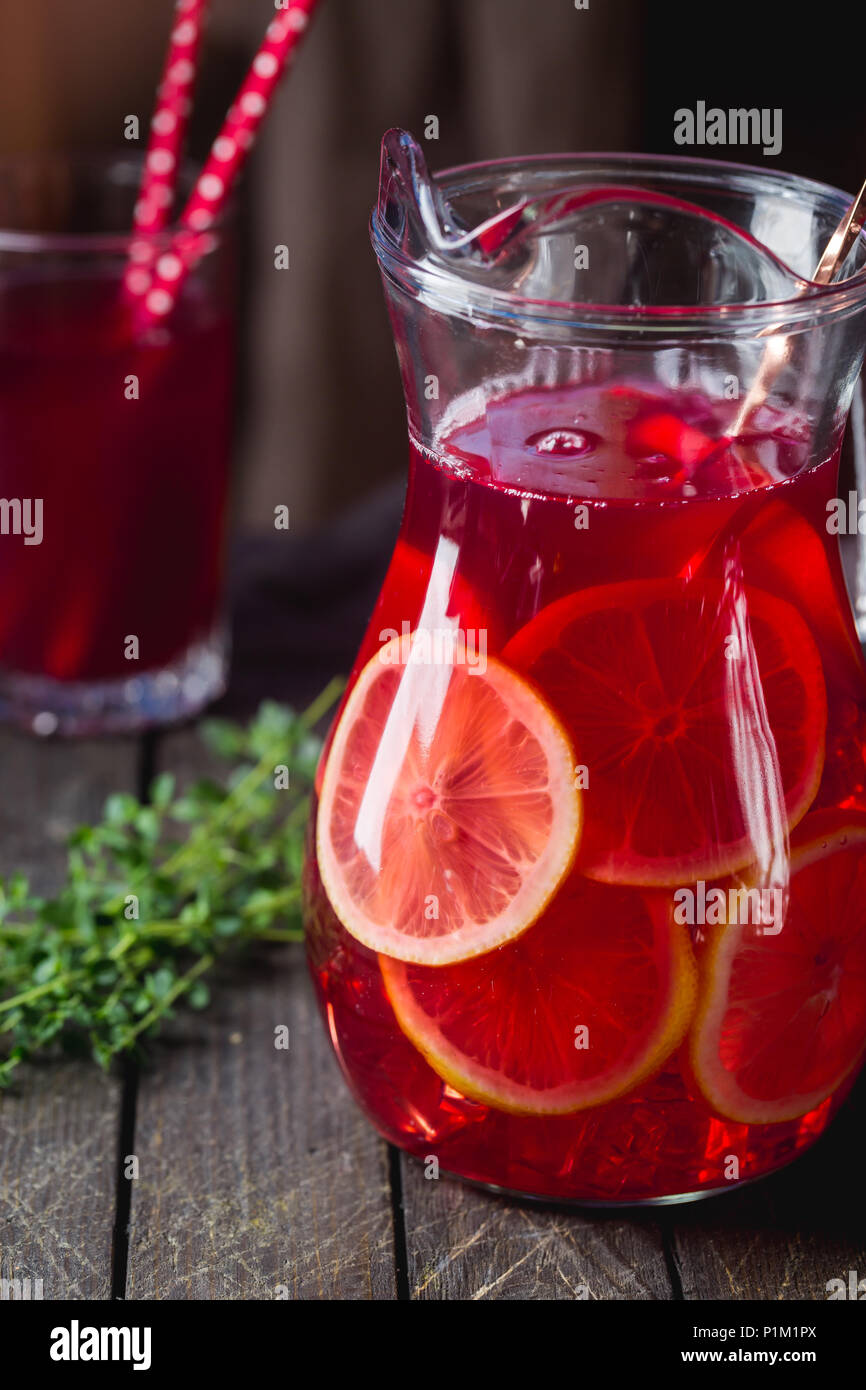 Red iced lemonade with sliced fresh lemons in a jug on dark wooden ...