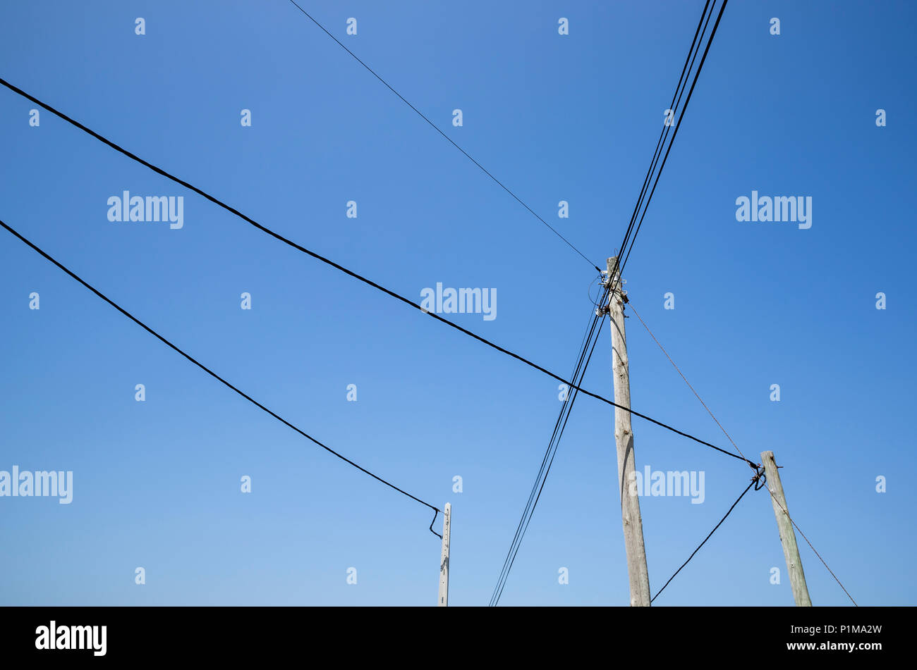 Three electricity poles and lines against a blue sky Stock Photo - Alamy