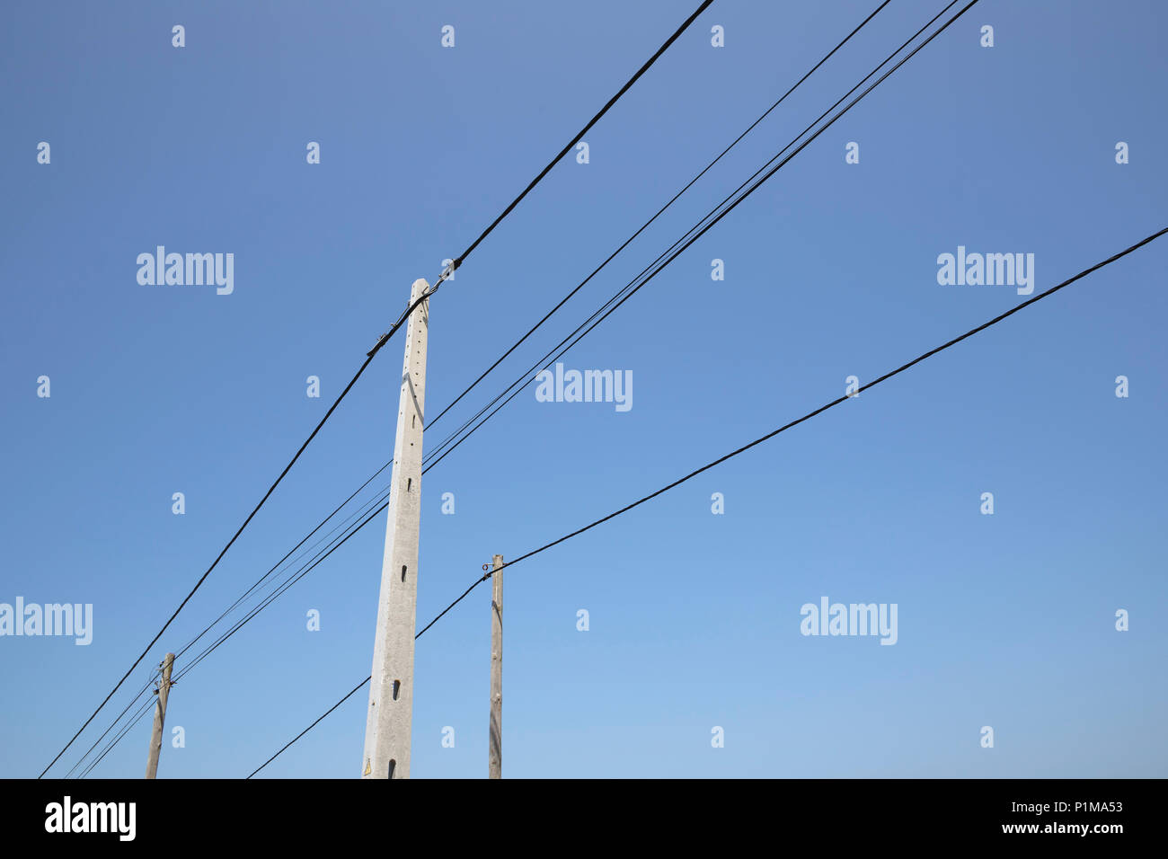 Three electricity poles and lines against a blue sky Stock Photo - Alamy