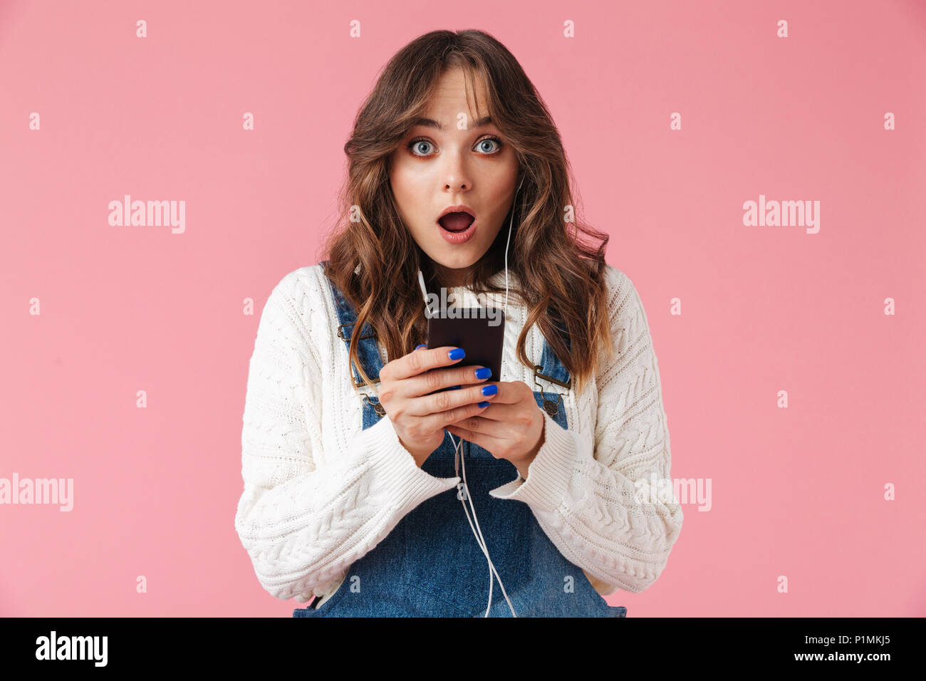 Portrait of a shocked young girl standing with earphones and mobile ...