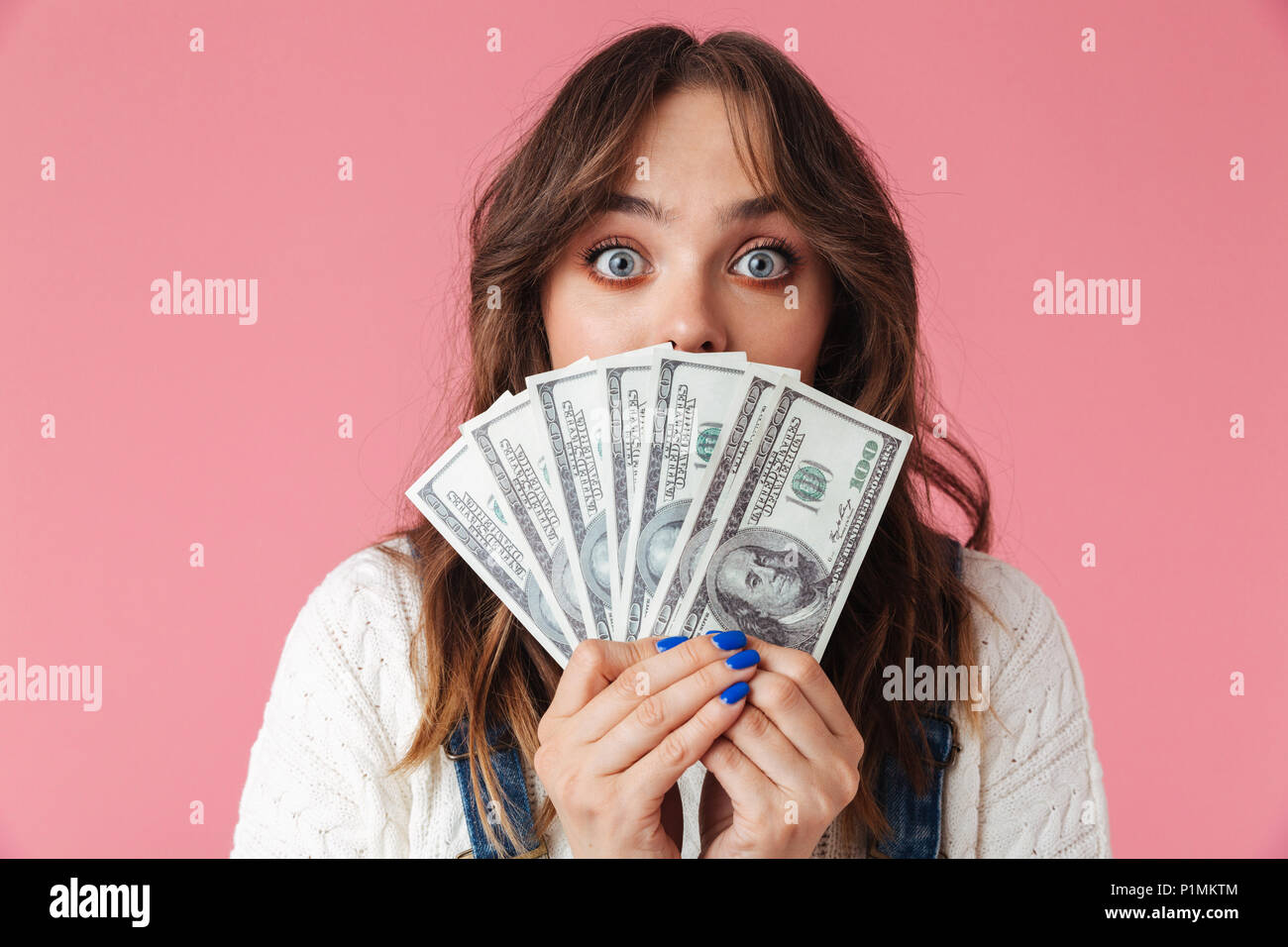 Portrait of a shocked young girl holding money banknotes isolated over ...