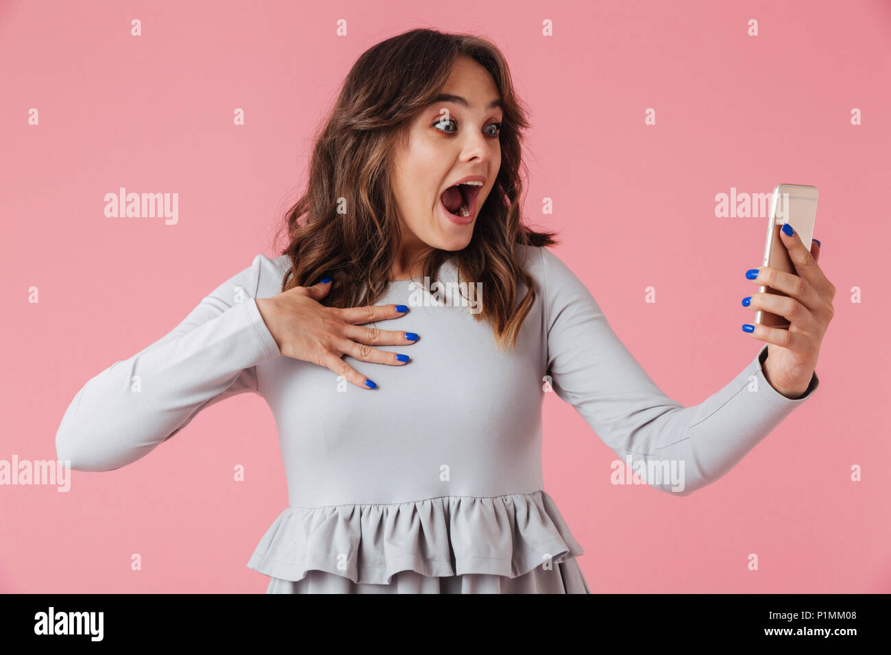 Portrait of a shocked young girl looking at mobile phone isolated over ...
