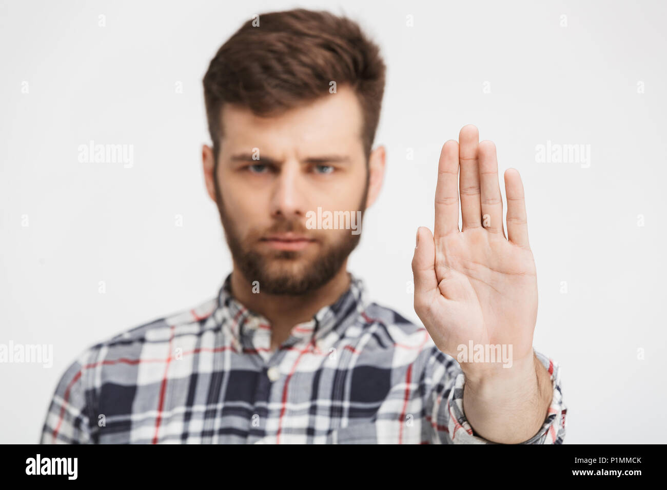 Portrait of a serious young man in plaid shirt showing stop gesture ...