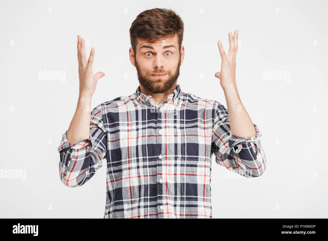 Portrait of a confused young man in plaid shirt looking at camera ...