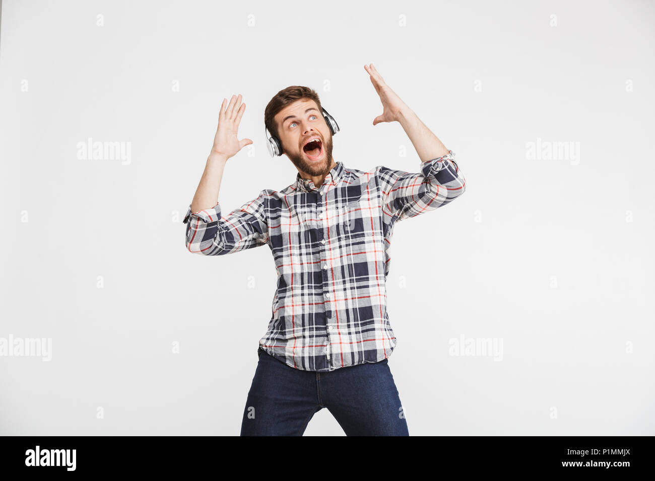 Portrait of an excited young man in plaid shirt listening to music with ...