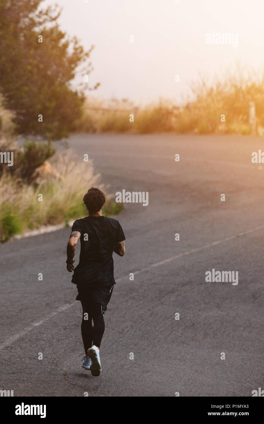 Healthy man running on mountain road. Rear view of athlete practicing ...