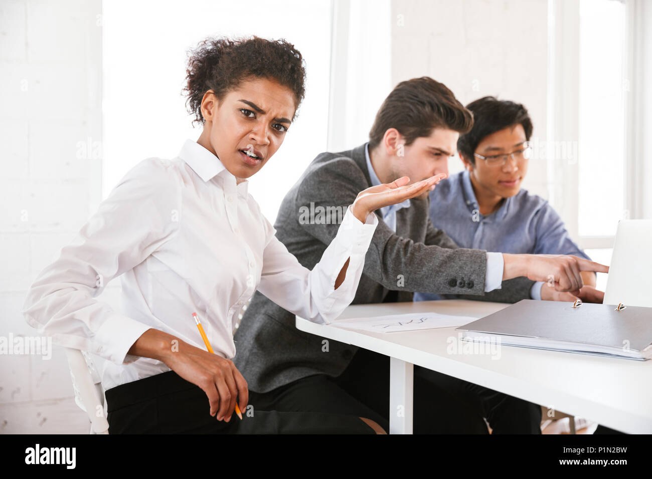 Confused young african woman sitting at the table with colleagues and ...