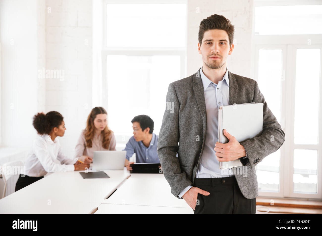 Confused young man holding laptop while standing at the table with ...