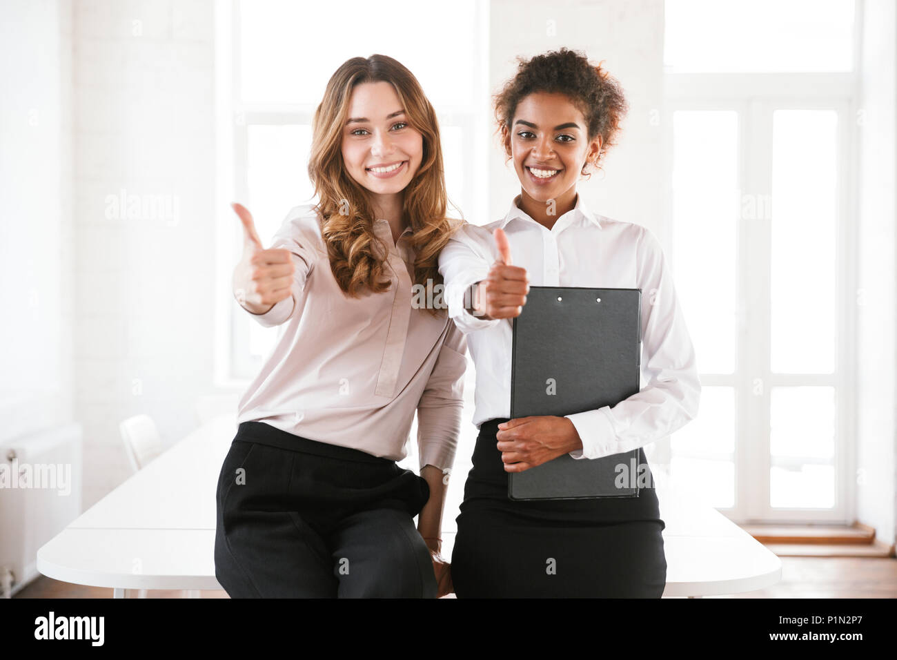 Two smiling business women sitting indoors with an open folder and ...