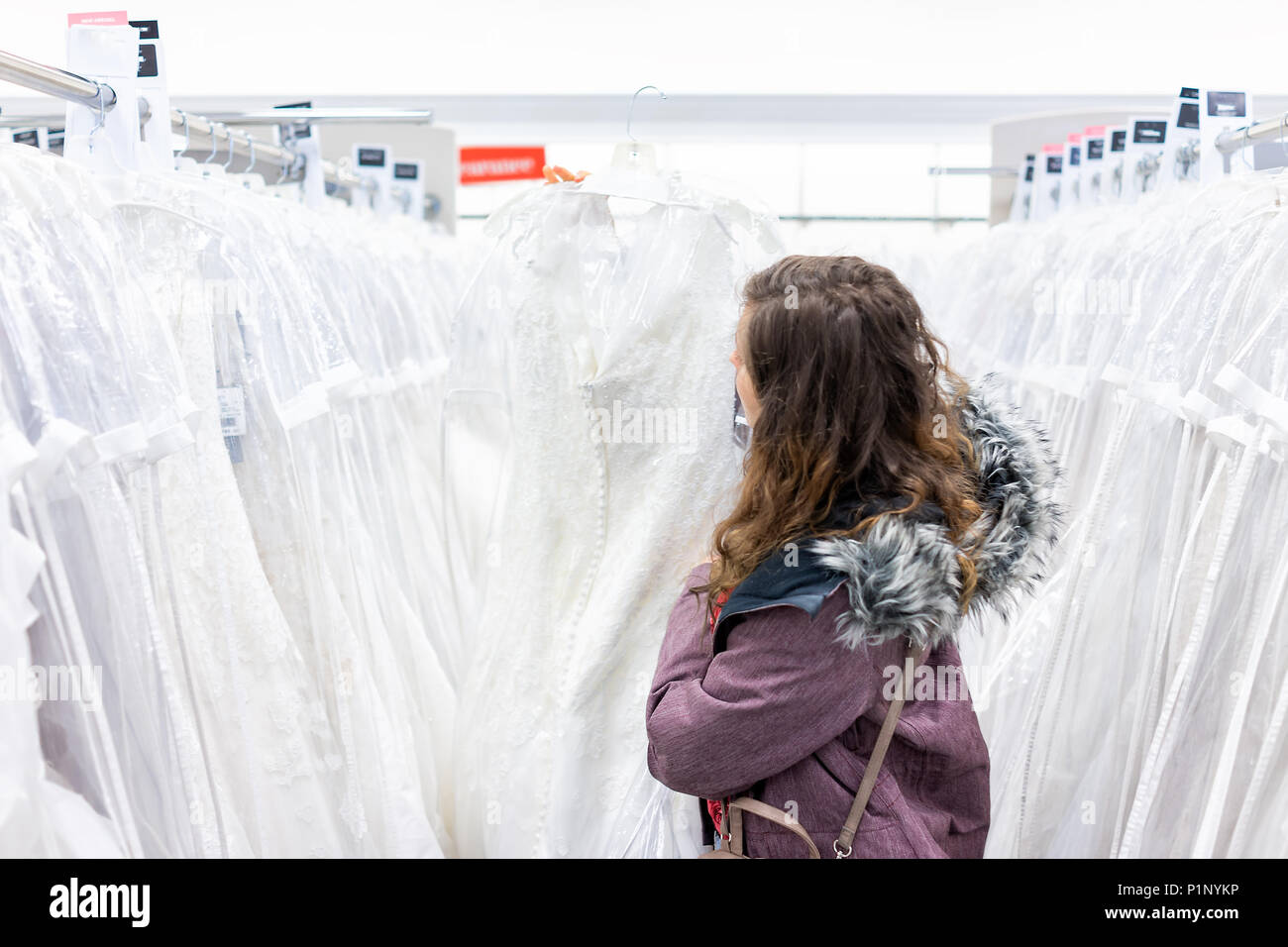 Young woman holding lace wedding dress in boutique discount store, many ...