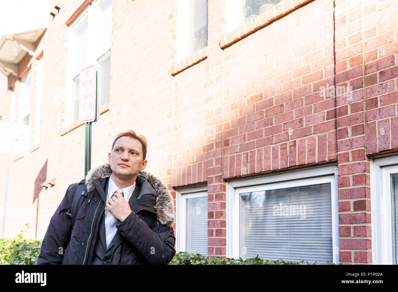 Young serious businessman face standing in front of brick wall, fixing ...