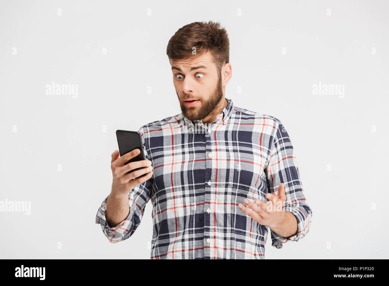 Portrait of a confused young man looking at mobile phone isolated over ...