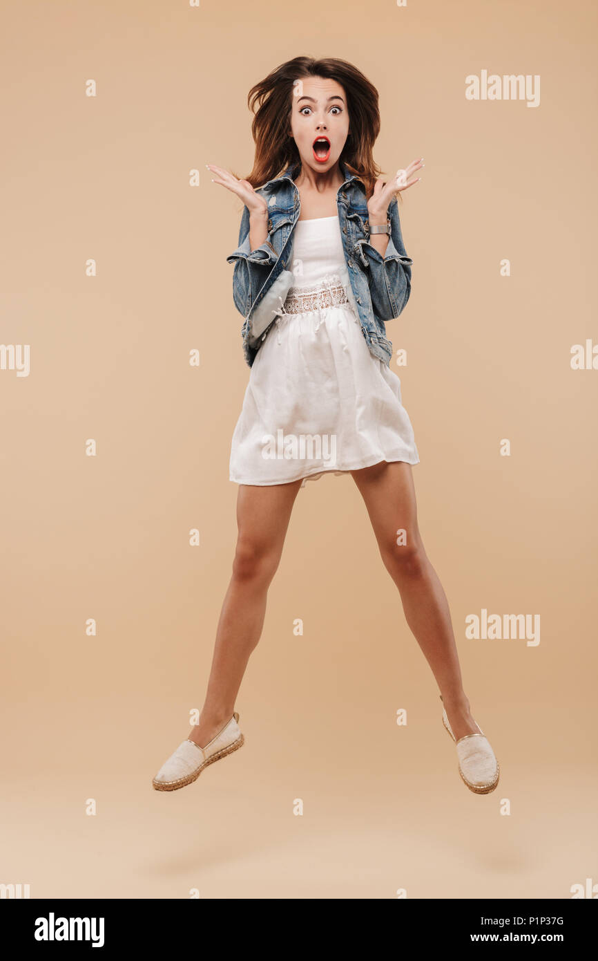 Full length portrait of a shocked young girl in summer clothes jumping ...