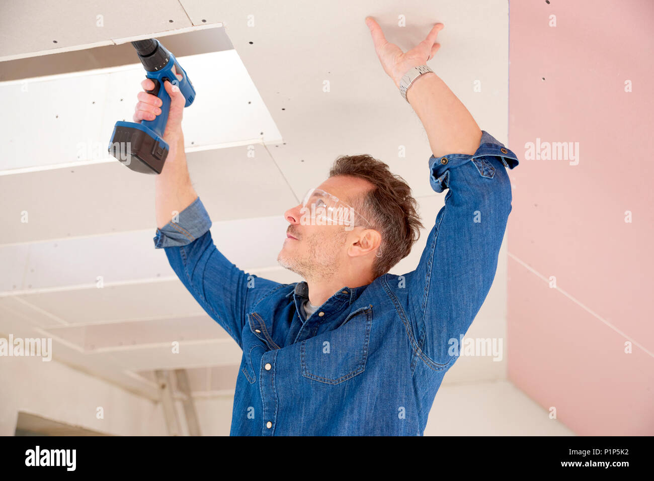 Handyman using cordless drill while working on construction site Stock ...