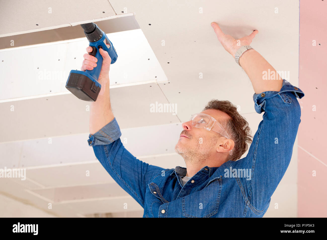 Handyman using cordless drill while working on construction site Stock ...