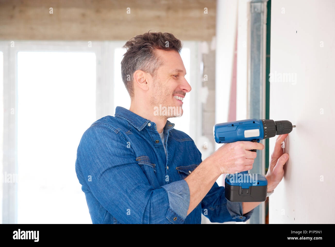 Handyman using cordless drill while working on construction site Stock ...